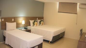 Quarto de hotel com duas camas de solteiro, uma mesa de cabeceira com luminária, uma pequena mesa e um ar condicionado fixado na parede.