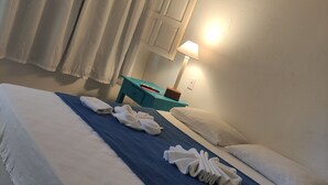 Quarto de hotel com cama, escrivaninha, luminária e janela com cortinas.