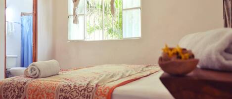 Um quarto com uma cama, uma janela com cortinas, uma toalha sobre a cama e uma mesa de madeira com uma tigela.