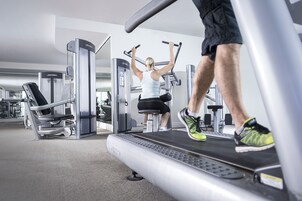 Uma academia com esteiras, aparelhos de musculação e uma pessoa usando barra fixa.