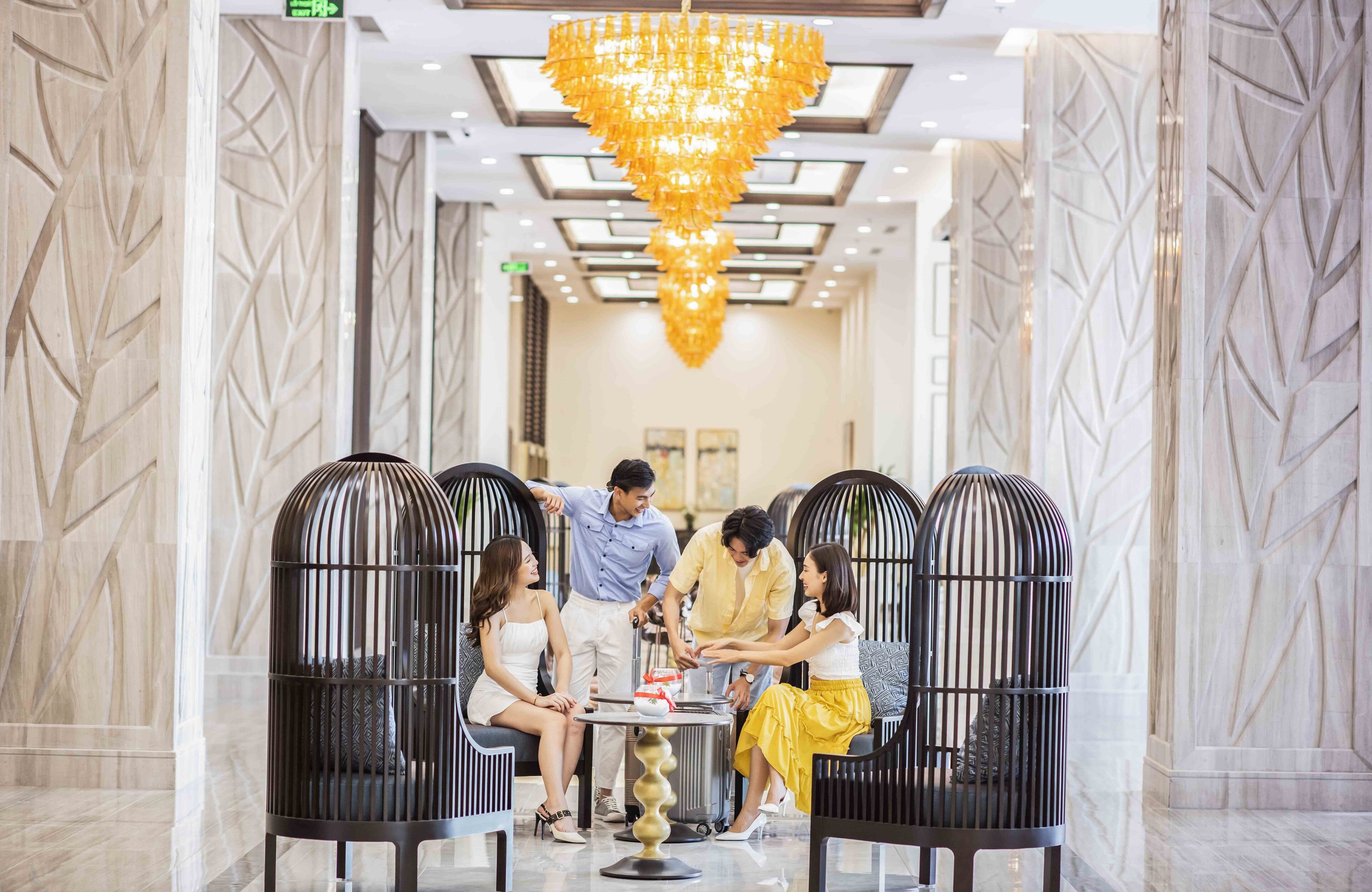 Um grupo de pessoas sentado em volta de uma mesa redonda num saguão com um candelabro moderno e design geométrico nas paredes.