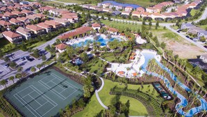Vista aérea de uma área residencial com uma grande piscina, quadras de tênis e um toboágua sinuoso.