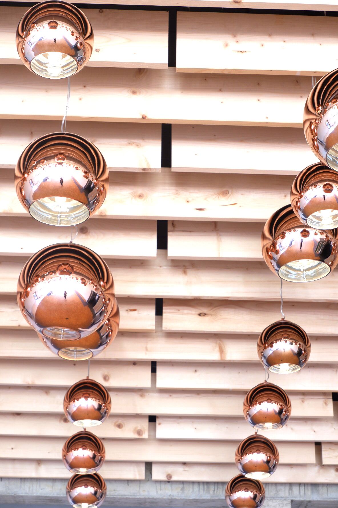 Diversas luminárias esféricas cor de cobre penduradas em um teto de ripas de madeira.