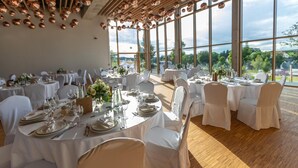Uma sala de banquetes com mesas redondas, toalhas brancas e cadeiras.