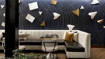 Um interior moderno com uma parede estampada, um sofá, uma mesa de jantar posta para dois e uma cadeira.