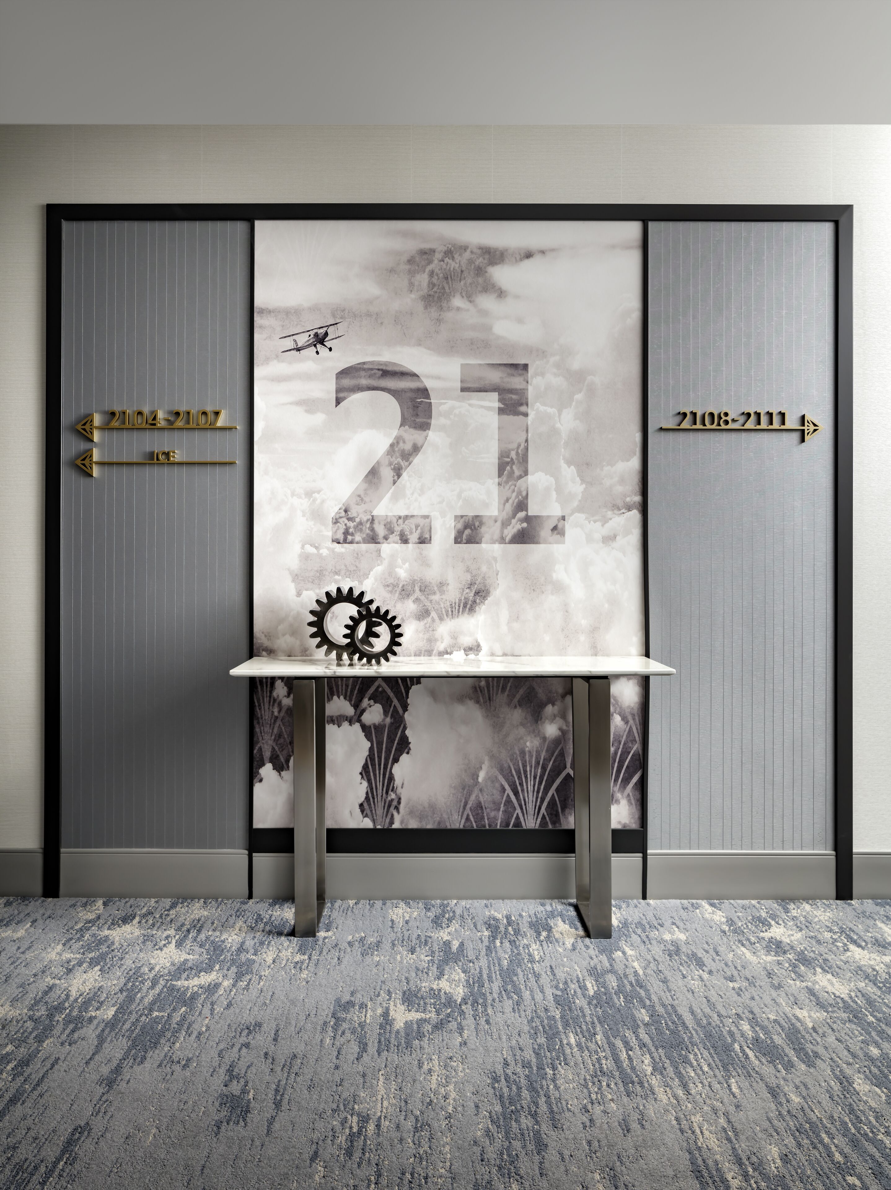 Quarto com o número '21' grande na parede, uma mesa com design de engrenagem e setas direcionais com números nas paredes.