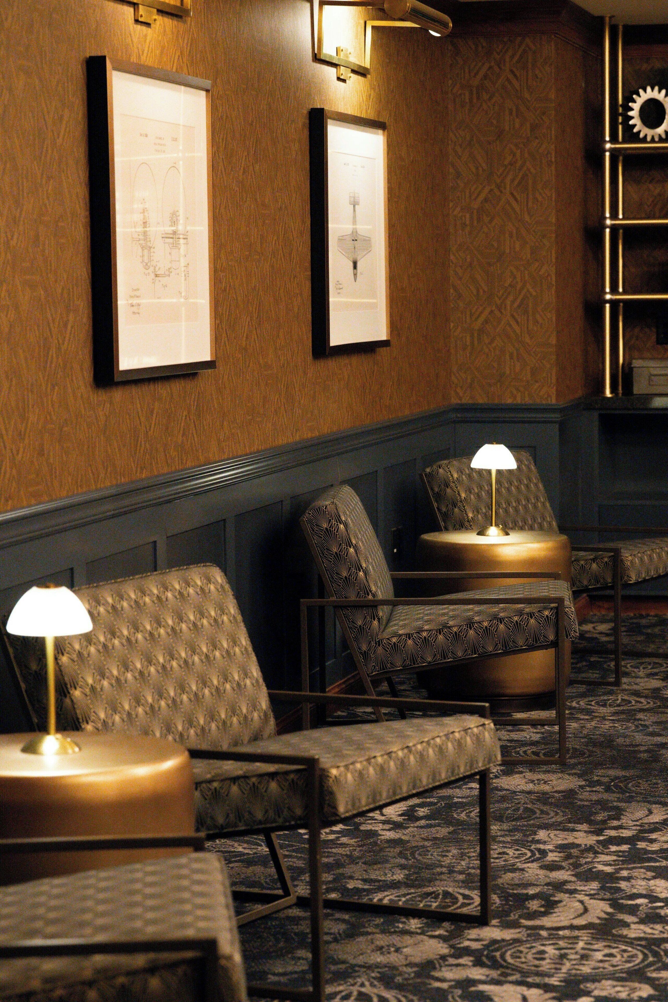 Um saguão de hotel com desenhos arquitetônicos emoldurados na parede, carpete estampado e áreas de estar com luminárias.
