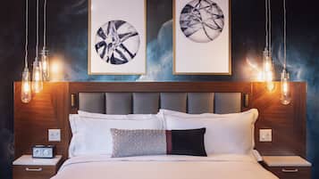 Cama bem arrumada com almofadas brancas e estampadas, cabeceira de madeira e duas obras de arte emolduradas acima.