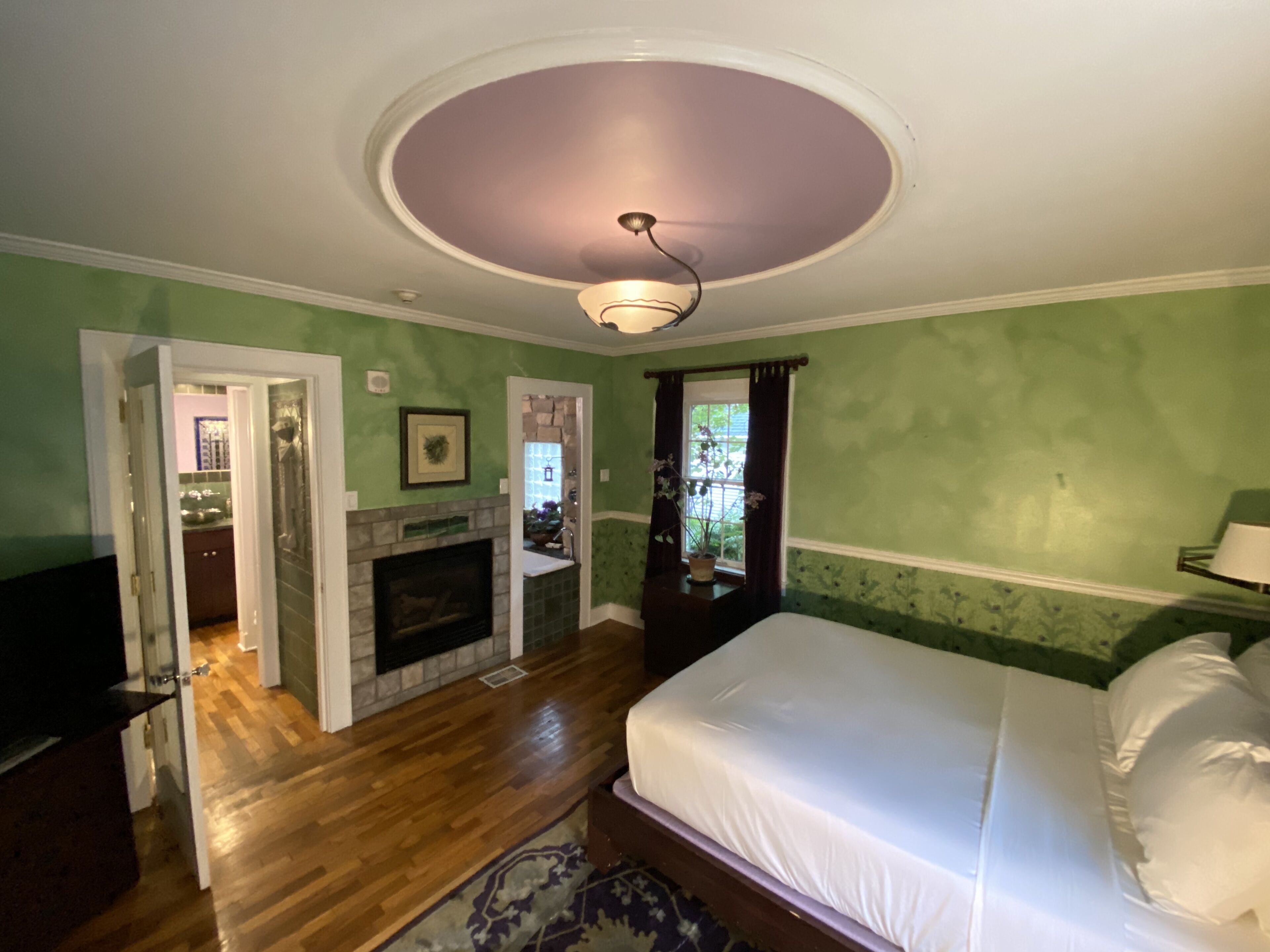Quarto com cama, lareira e vista para um jardim através de uma janela.