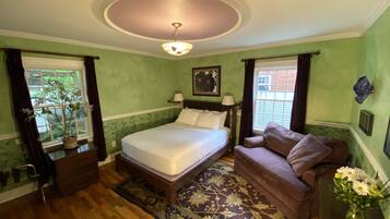 Quarto com cama, mesa de cabeceira, cômoda, janela com cortinas, luminária no teto, um quadro na parede e tapete estampado.