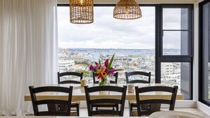Uma sala de jantar com uma mesa, cadeiras e vista para a cidade através de grandes janelas.
