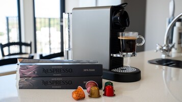 Uma máquina de café Nespresso com uma chávena de vidro, duas caixas de Nespresso e três cápsulas sobre uma bancada de cozinha.