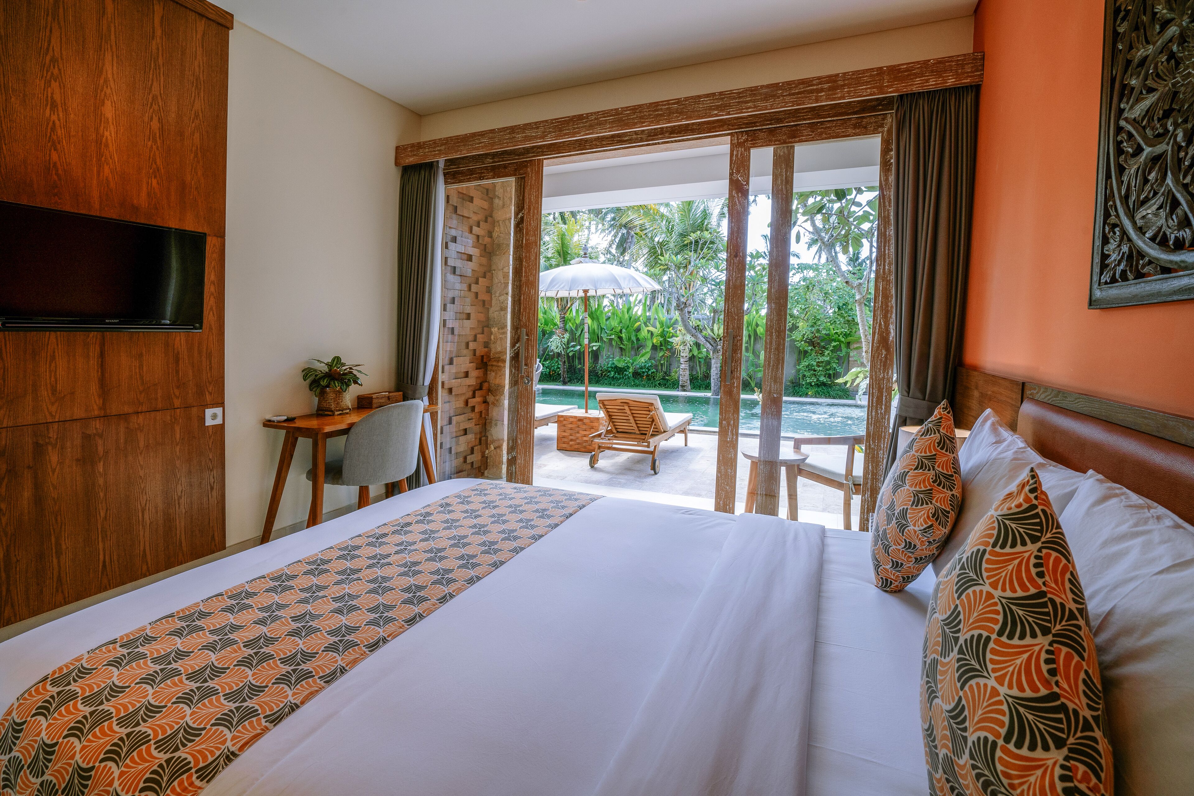 Quarto de hotel com uma cama grande, uma televisão na parede, uma pequena mesa de trabalho com uma cadeira e vista para a área da piscina.