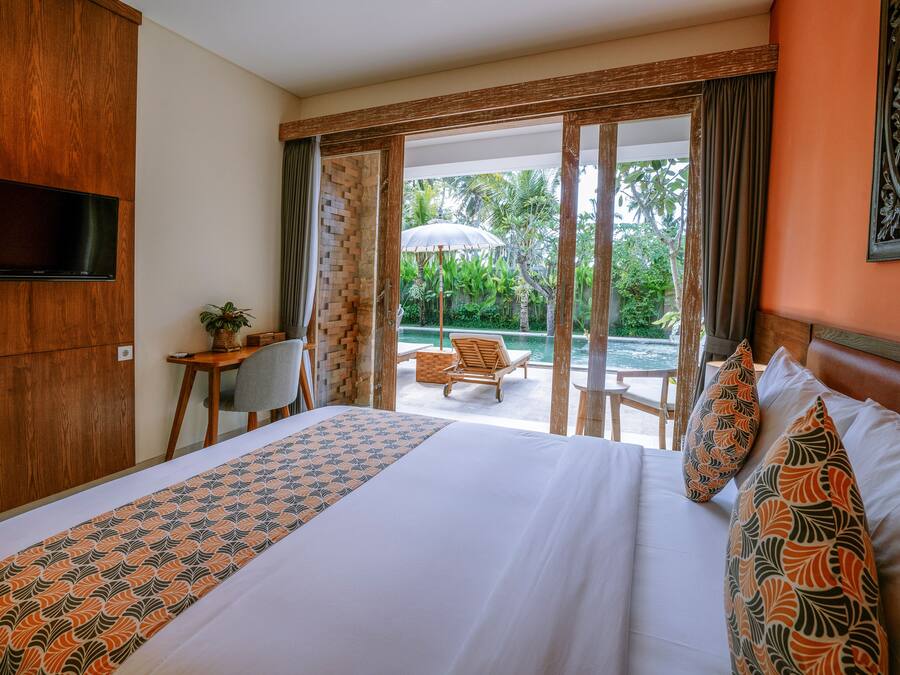 Quarto de hotel com uma cama grande, uma televisão na parede, uma pequena mesa de trabalho com uma cadeira e vista para a área da piscina.