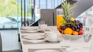 Uma área de jantar moderna com uma mesa posta para dois, uma fruteira e vista para o exterior.