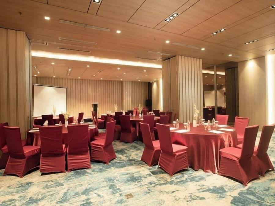 Uma sala de conferências com mesas redondas e cadeiras vermelhas, teto de madeira e piso coberto por carpete.