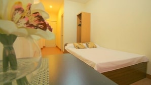Quarto pequeno e bem arrumado com uma cama de solteiro, mesa de cabeceira e uma cadeira.