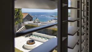 Uma varanda com vista para o oceano, uma pequena área de jardim com lareira e um edifício com um design arquitetônico único.