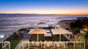 Terraço no telhado com área de estar ao ar livre e vista para o oceano ao pôr do sol.