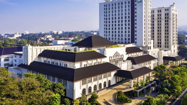 Hotel moderno com um pátio central, rodeado por vegetação exuberante e vista para o horizonte urbano.