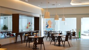 Um restaurante moderno com mesas e cadeiras de madeira, iluminação pendente e uma grande janela com vista.