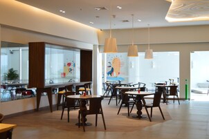 Um restaurante moderno com mesas e cadeiras de madeira, iluminação pendente e uma grande janela com vista.