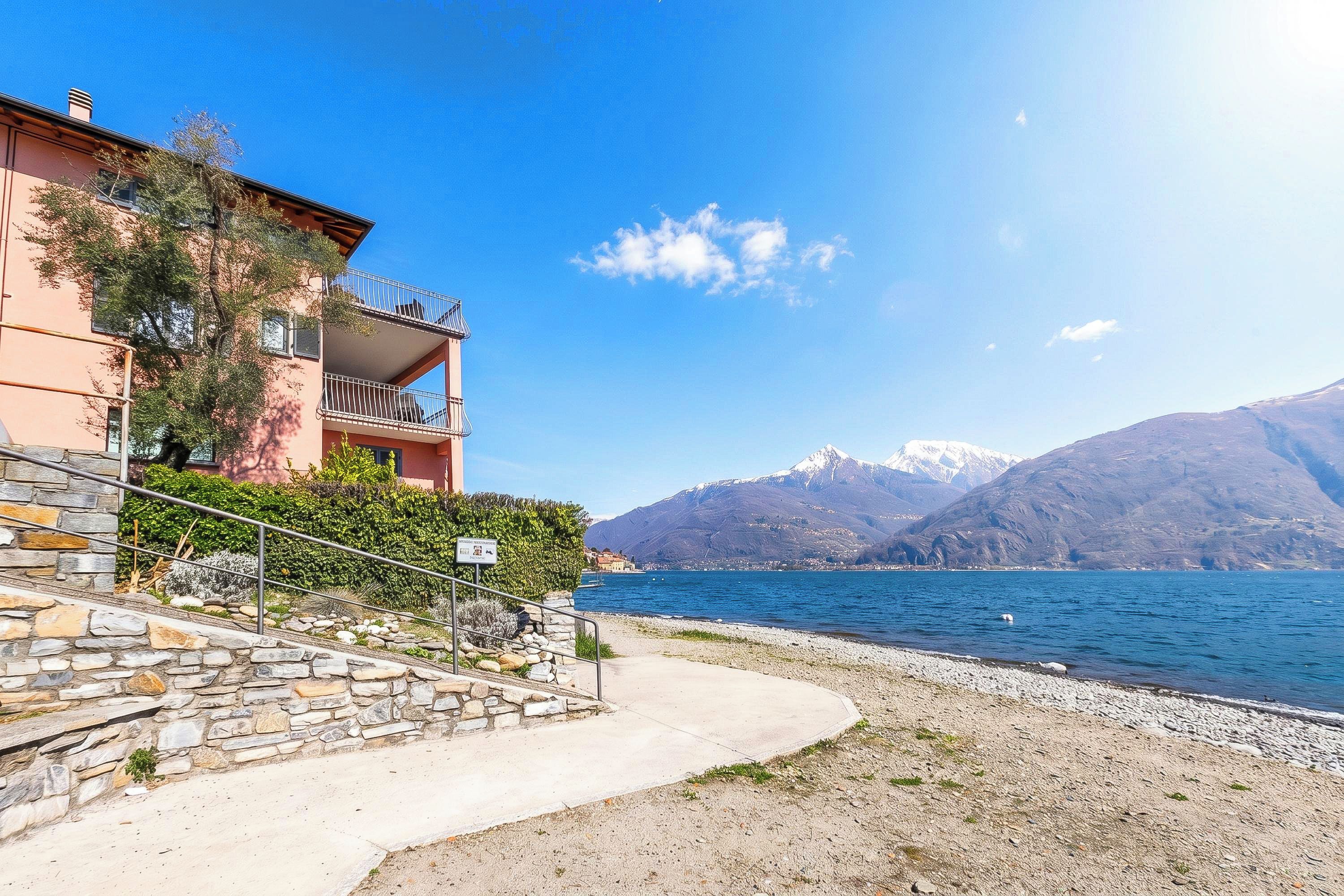 Um edifício costeiro com escadaria de pedra que leva a uma varanda, com vista para um lago e montanhas ao fundo.