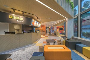 Interior de café moderno com balcão de recepção, área de estar e um mural colorido na parede.
