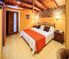 Quarto com cama, piso de madeira, parede de pedra e uma porta.