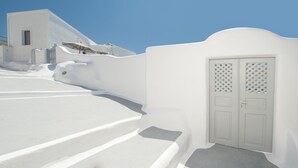 Um edifício branco com porta e janela, rodeado por paredes brancas e um céu azul límpido.