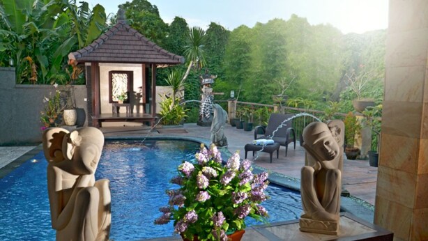 Área de piscina com estátuas, um gazebo e vegetação exuberante.
