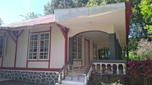 Um edifício com base de pedra, fachada vermelha e branca, e varanda coberta com uma escadaria.