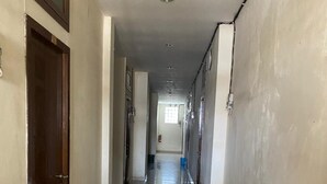 Um corredor com uma porta à esquerda, um banco ao centro e uma lixeira à direita.