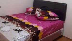 Quarto pequeno com cama coberta por edredom floral, cabeceira preta e parede branca lisa.