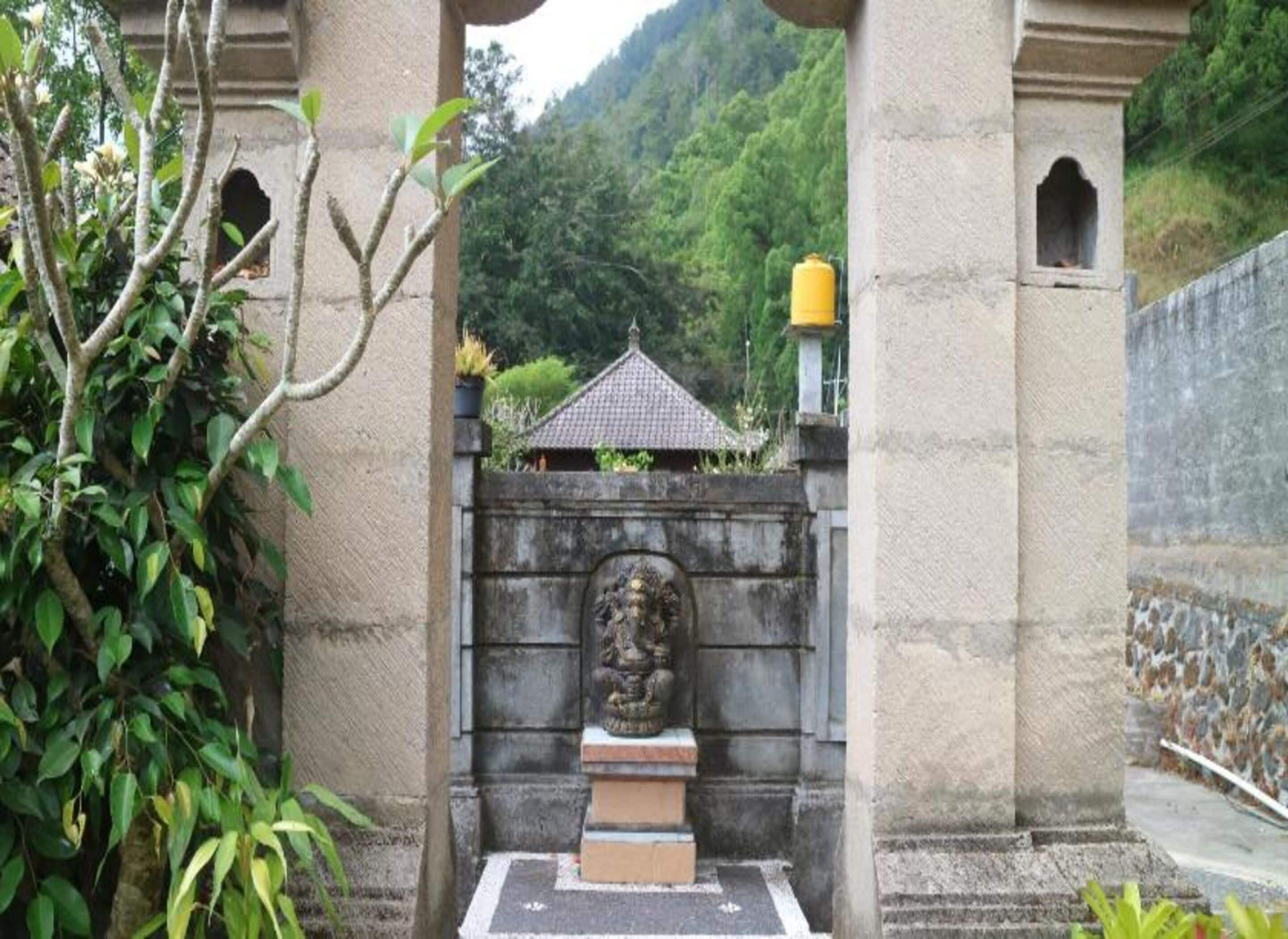 Um portão de pedra com estátua de leão, que dá acesso a uma construção tradicional com telhado de azulejos.