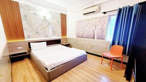 Quarto de hotel com cama, uma cadeira, televisão e janela com cortinas.