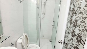 Um banheiro moderno com chuveiro em box de vidro, vaso sanitário e pia.
