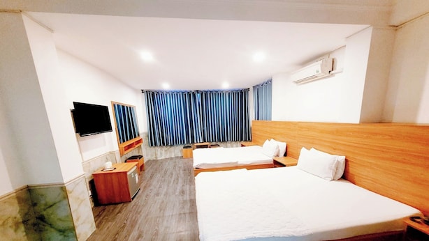 Quarto de hotel com duas camas, uma escrivaninha, televisão e banheiro.