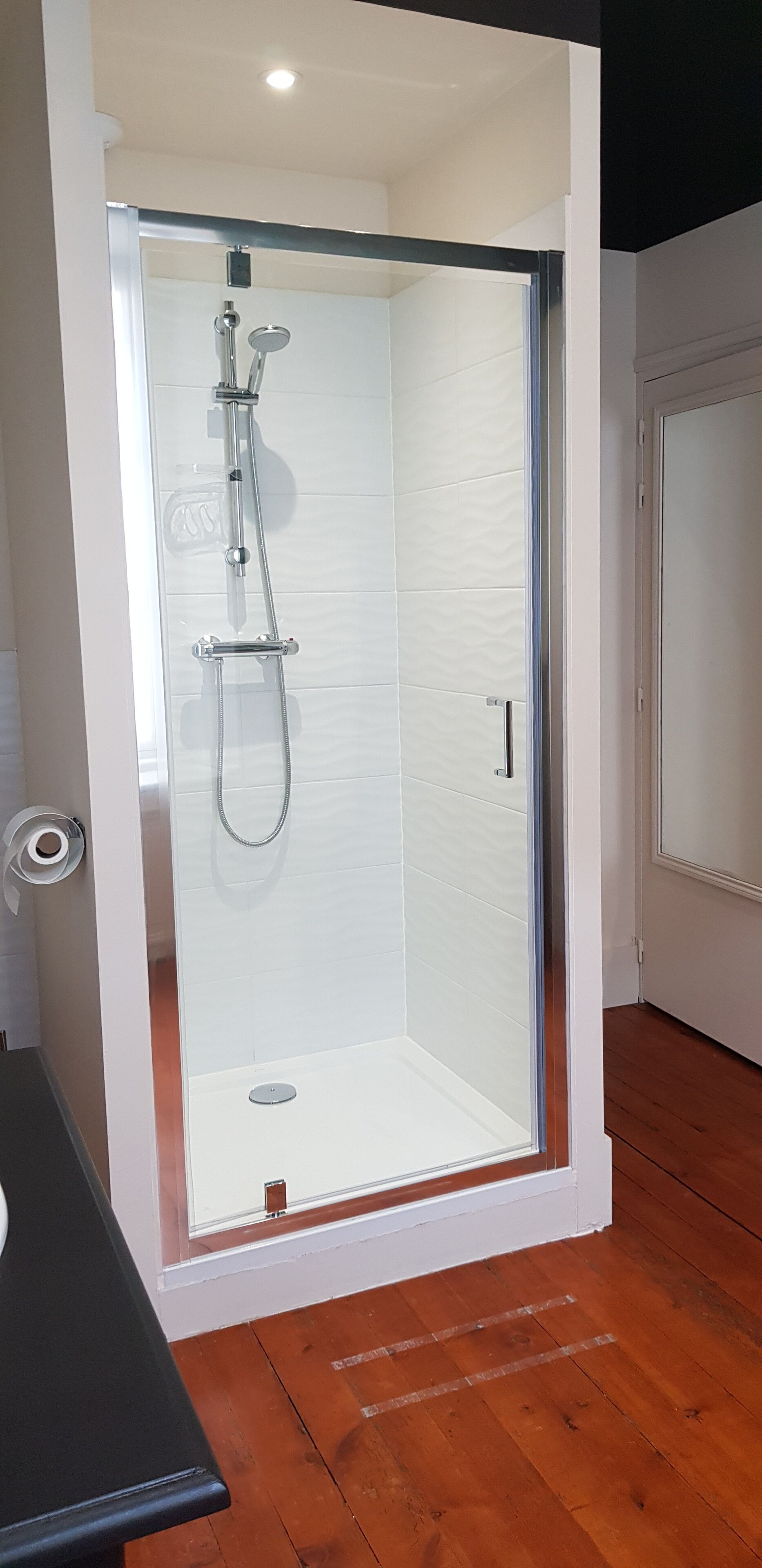 Box de chuveiro moderno com porta de vidro, chuveiro manual e torneira embutida na parede.