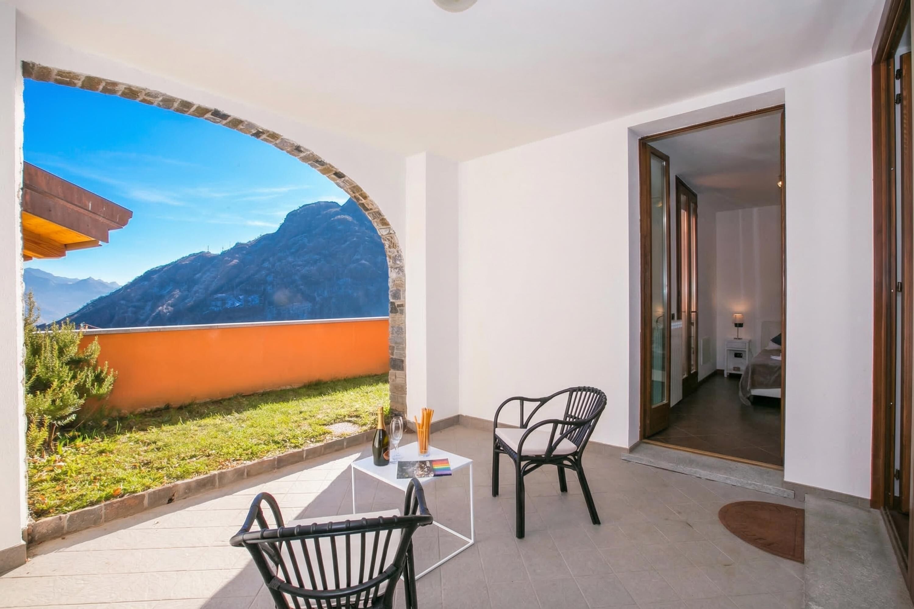 Varanda com vista para montanhas, uma mesa com cadeiras e uma porta de entrada para um quarto.