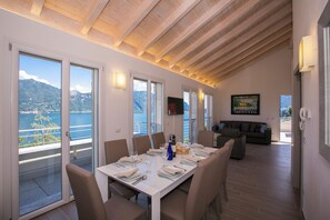 Uma sala de jantar com mesa posta para seis pessoas, grandes janelas e vista para o mar.