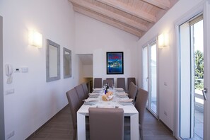 Uma área de refeições com uma mesa branca posta para seis pessoas, rodeada por cadeiras, com um cartaz emoldurado na parede e um telefone também na parede.