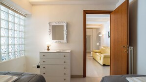 Quarto com duas camas, cômoda, espelho e porta que dá para outro ambiente.