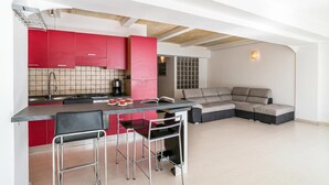 Cozinha moderna com armários vermelhos, área de refeições com banquetas de bar e um sofá modular cinza.