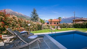 Piscina com espreguiçadeiras, deck de pedra e vista para as montanhas.