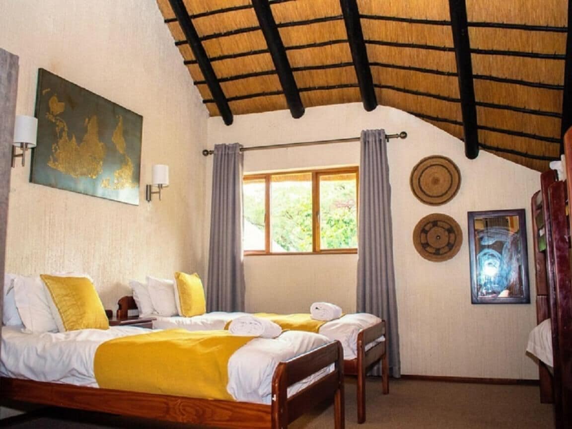 Quarto com duas camas, janela com cortinas, luminária na parede e um quadro.