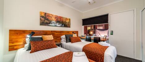 Quarto de hotel com duas camas, um ventilador de teto, uma pintura de uma cascata e uma mesa com um computador.