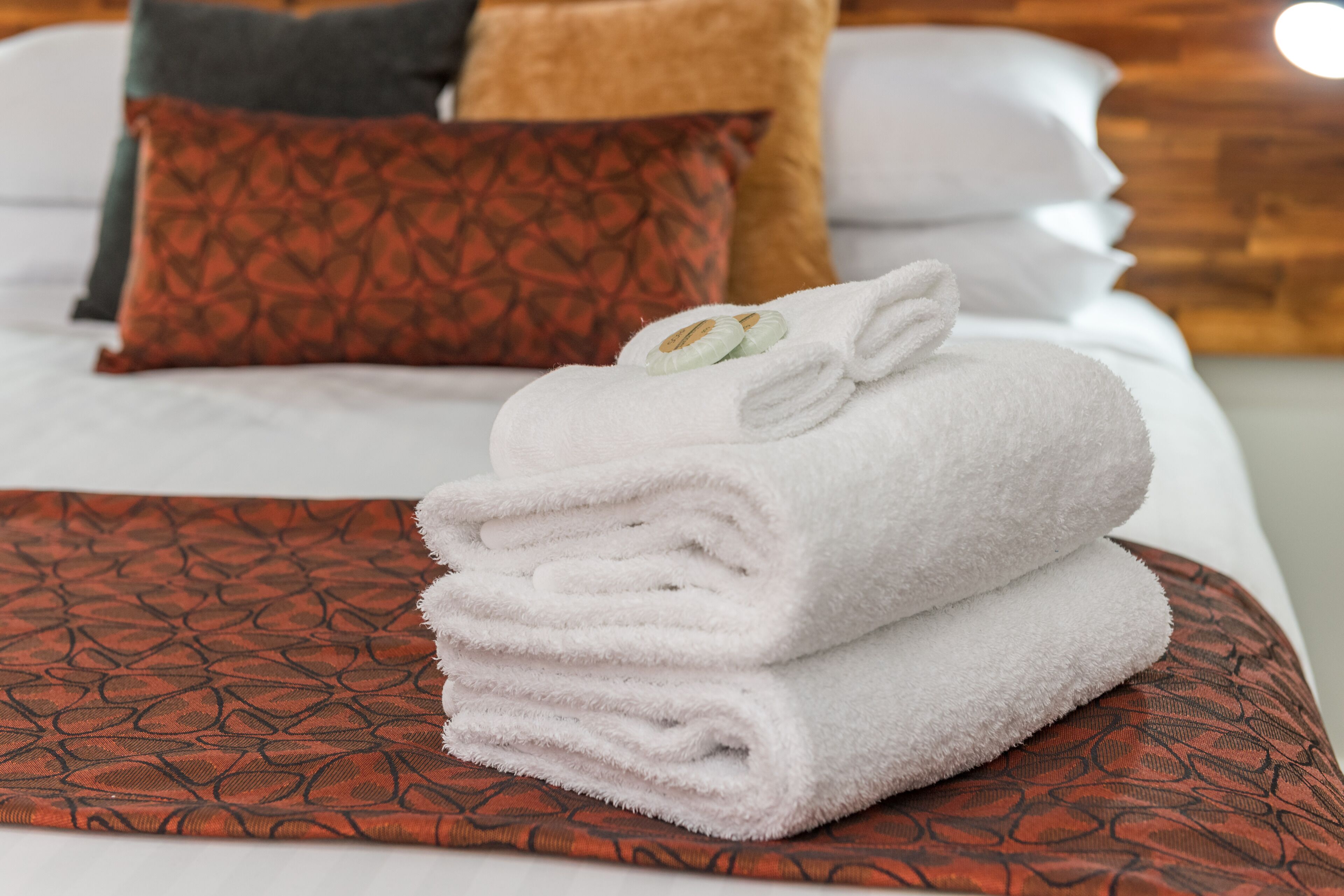Cama bem arrumada com uma pilha de toalhas brancas sobre um cobre-leito vermelho e preto estampado.