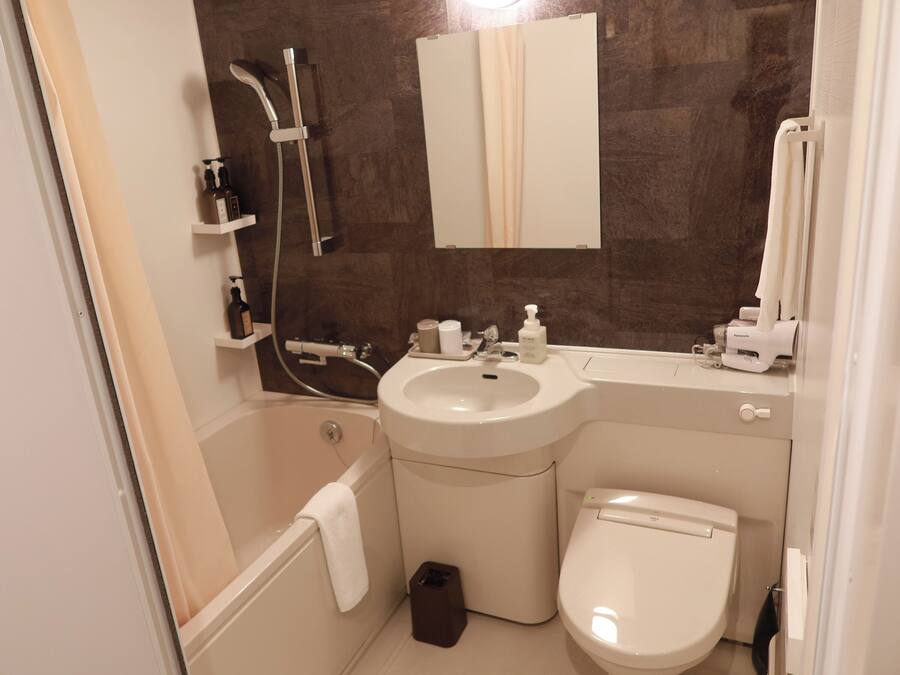 Uma casa de banho moderna com banheira, lavatório e sanita. Inclui um chuveiro, um porta-toalhas e um dispensador de sabonete.