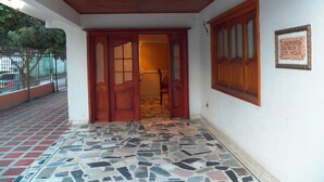Entrada de um edifício com chão de azulejos, portas de madeira e uma placa na parede.